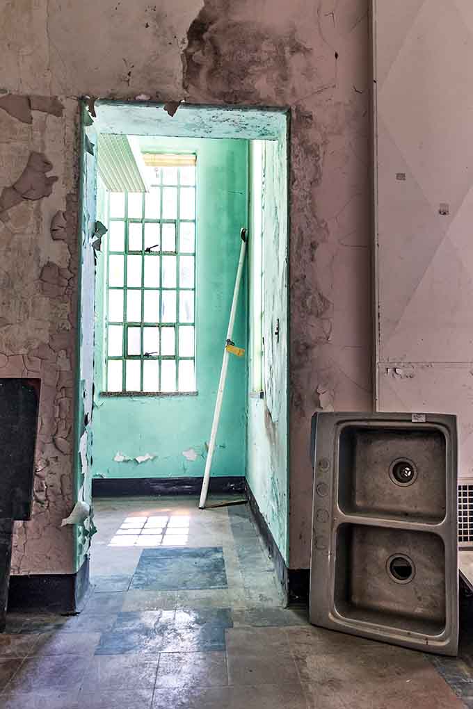 Mint-green walls, a stray mop handle, and a disconnected sink somehow make this doorway look like a surrealist painting.
