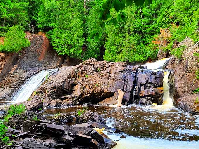 Rust-colored rock formations frame twin cascades, proving that geology can be just as dramatic as any waterfall.
