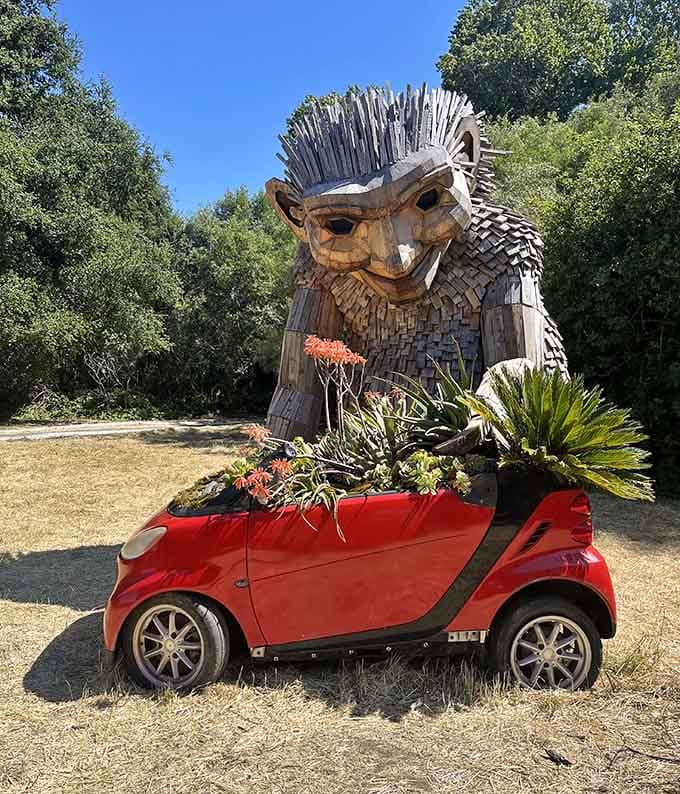 A massive wooden troll peering curiously into a tiny red car filled with succulents. Honestly, same energy as most San Francisco commuters.