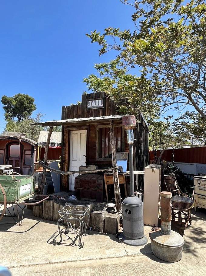 A weathered old jail facade surrounded by vintage ironware and outdoor relics, looking like a movie set that never got torn down.