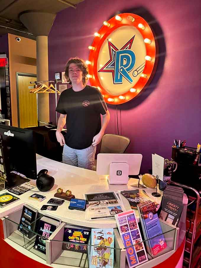 The welcoming face behind the front desk, framed by that glowing marquee logo, sets the tone perfectly from the moment you arrive.
