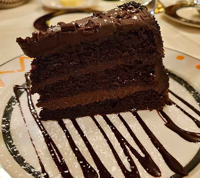 Three layers of dark chocolate cake with chocolate frosting, drizzled on a plate that knows exactly what it's doing.