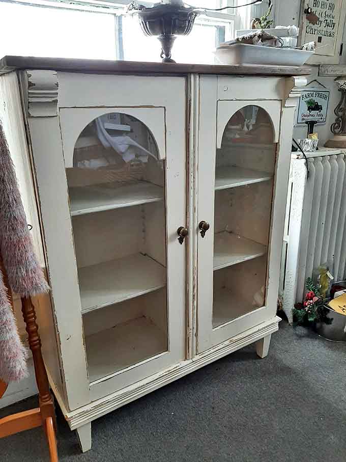 A cream-painted cabinet with arched glass doors that looks like it escaped from a very elegant farmhouse.