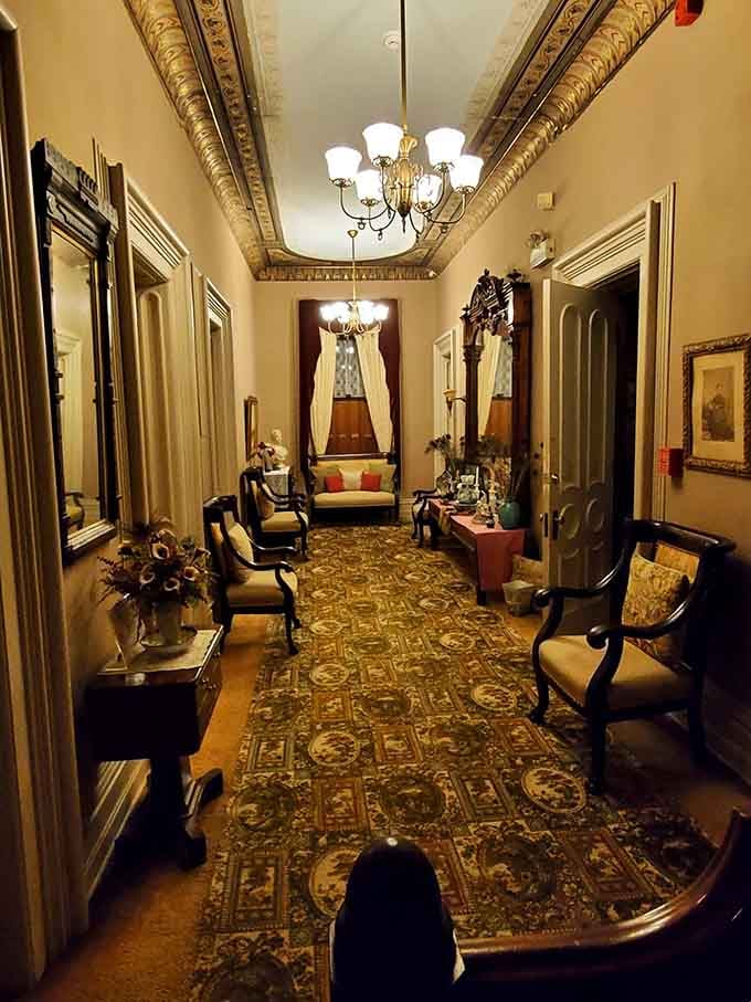 A long hallway lined with antique chairs, ornate rugs, and soft chandelier light. Walking through here feels like moving through a very elegant time machine.