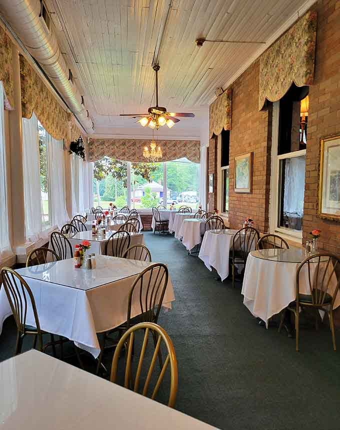 The enclosed porch dining room with floral valances, exposed brick, and white tablecloths feels like eating inside a very well-dressed sunroom.