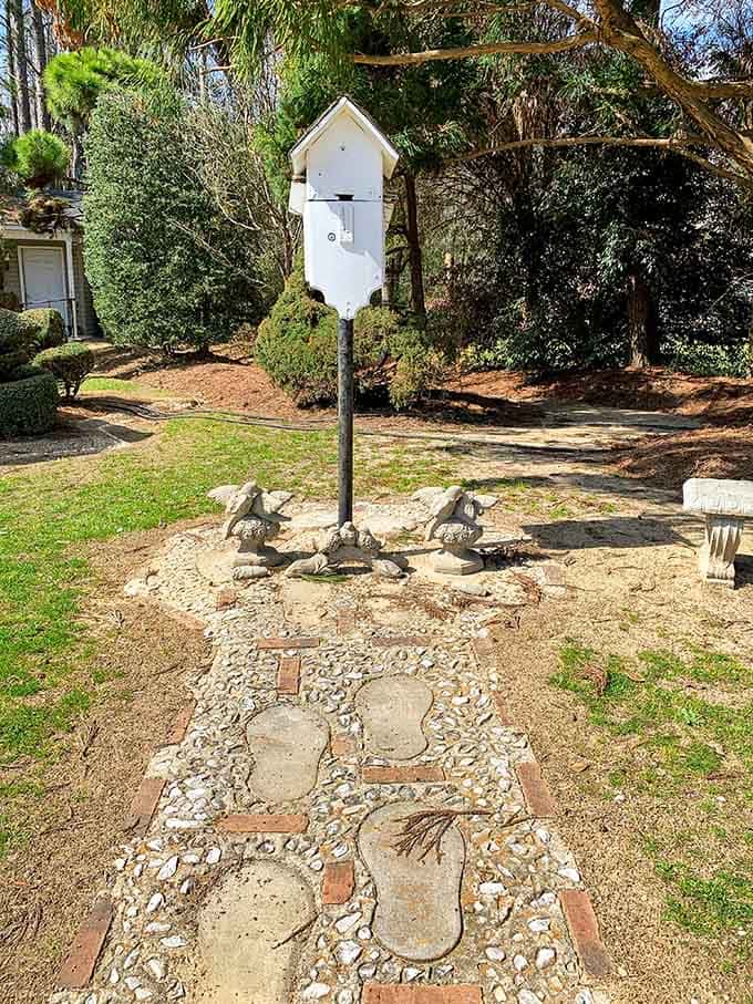 Concrete footprints lead right up to a charming birdhouse on a pole, flanked by small stone figures keeping quiet watch.