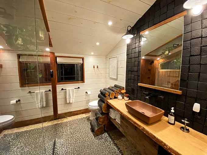 Stacked log towel holders, a live-edge wood vanity, and pebble tile floors, this bathroom quietly outclasses most hotel spas.