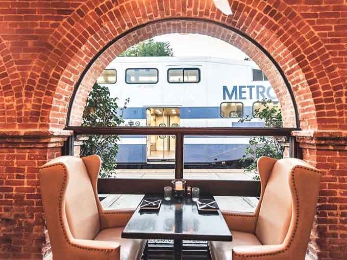 Two leather chairs, a dark table, and a Metrolink train rolling past a brick arch. Best seat in California, arguably.