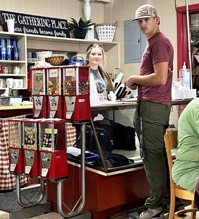 A smiling face behind the counter surrounded by gumball machines and a sign reading "The Gathering Place" &mdash; that sign is absolutely right.
