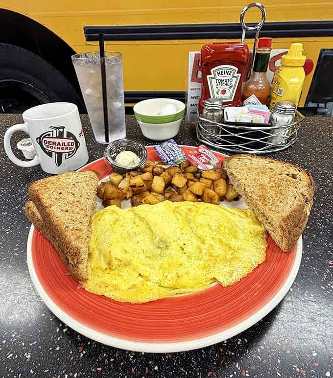 A big, fluffy omelet with home fries and toast, served in a Derailed Diner mug. Breakfast here is not a small commitment.