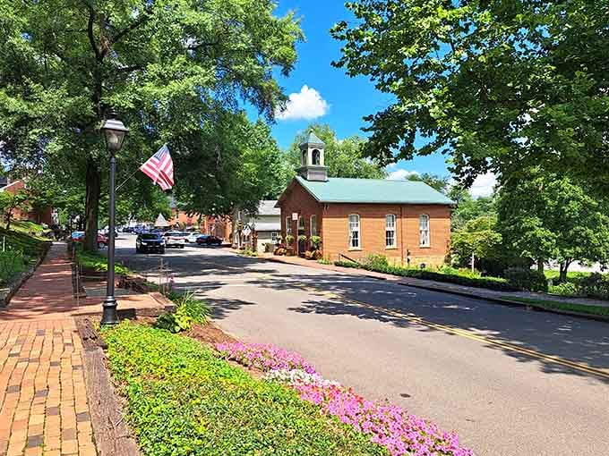 A brick church with a green steeple anchors this sun-drenched street like the calm center of a very good dream.