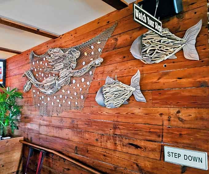 Driftwood fish sculptures and fishing nets on warm wooden walls. The decor tells the whole coastal story.