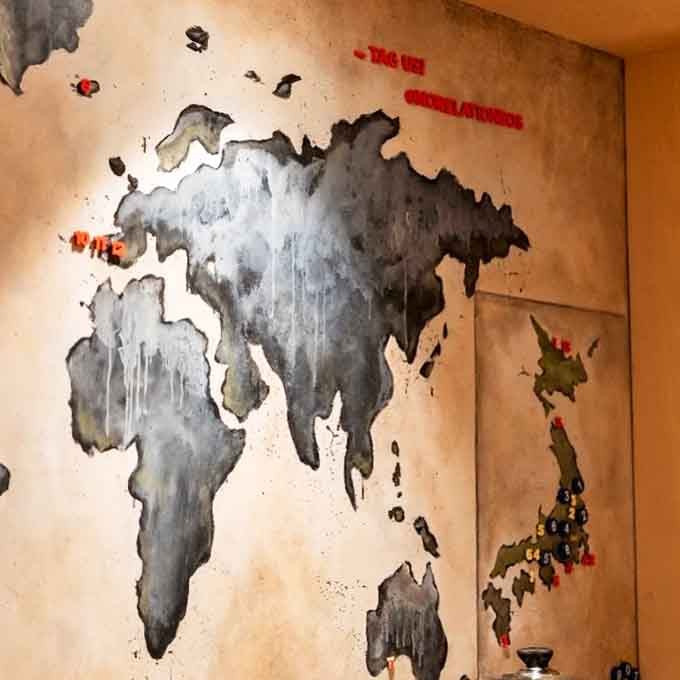 That moody world map mural stretches across the wall like a quiet promise that the flavors arriving at your seat have traveled far to find you.