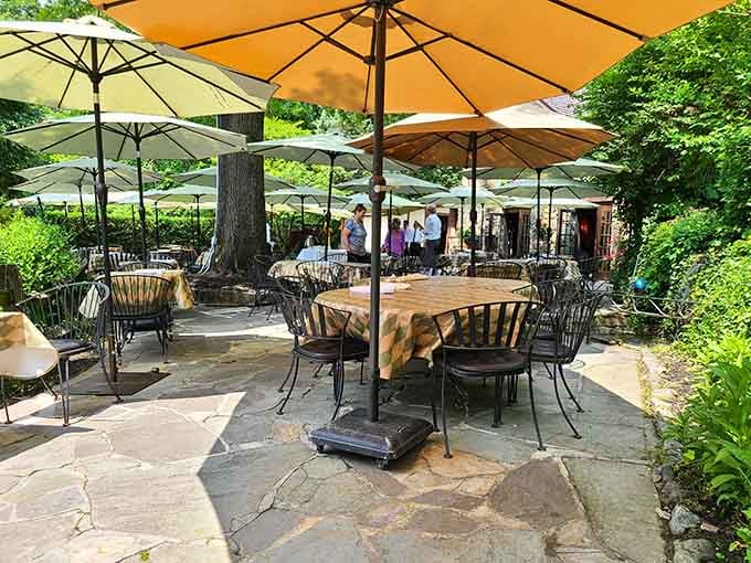 Flagstone paths, golden umbrellas, and lush green trees overhead create an outdoor dining space that feels genuinely enchanted.