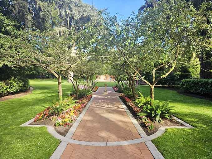 A brick pathway lined with flowers and framed by arching trees, the kind of garden path that makes you slow your whole life down.