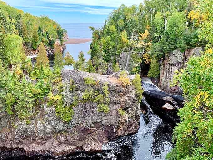 Massive basalt columns rise above a dark rushing river, with Lake Superior shimmering in the distance like a well-earned reward.