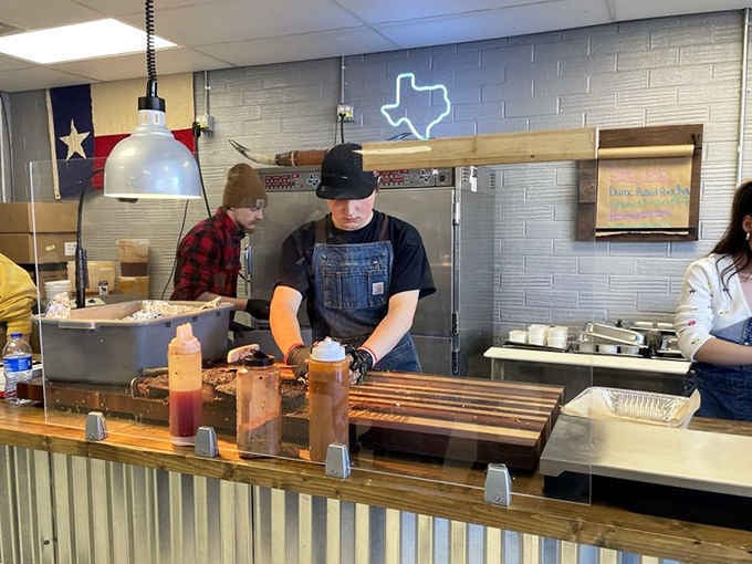 Behind the corrugated steel counter, focused hands are slicing brisket. This is craft, not just cooking.