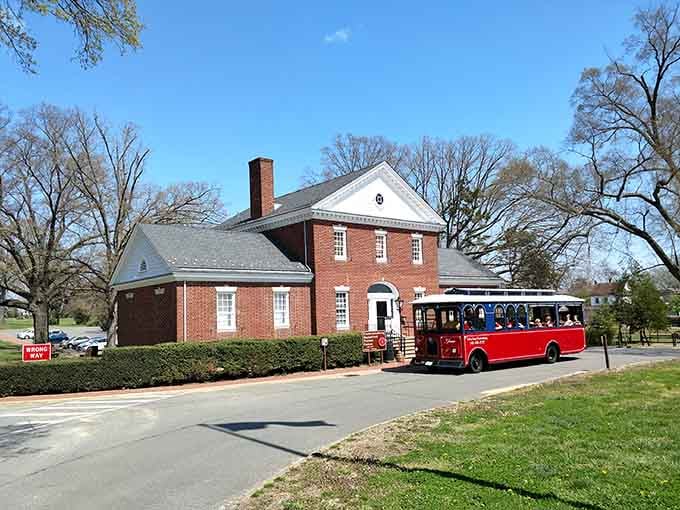 The trolley pulls up alongside a handsome brick colonial building under a wide blue sky, looking like it belongs on a Virginia postcard.
