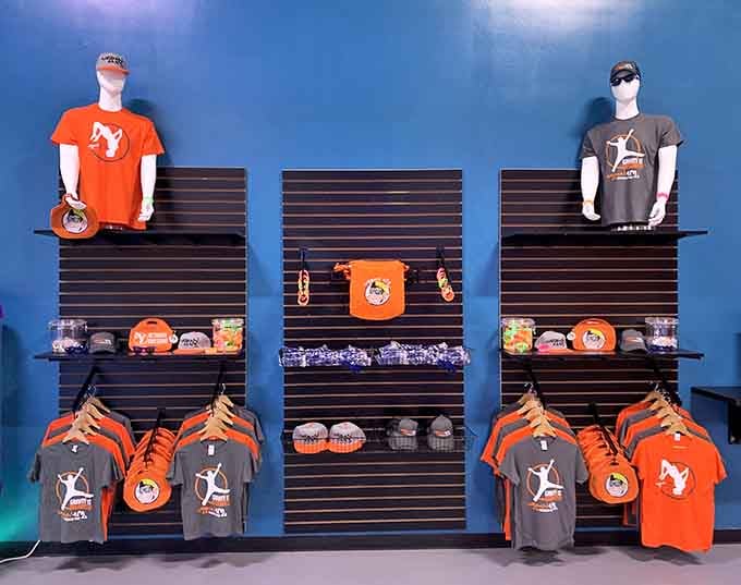 Orange and gray gear fills the merch wall, because apparently conquering a warrior course deserves a souvenir t-shirt.