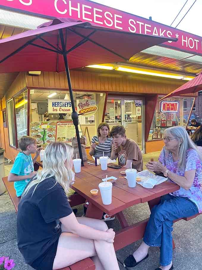 Families gathered around red picnic tables, food in hand, smiling. This is exactly what a good drive-in looks like.