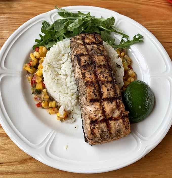 Grilled salmon with perfect char marks, lime rice, corn salsa, and fresh arugula. This plate is what happens when a kitchen genuinely cares about every dish.