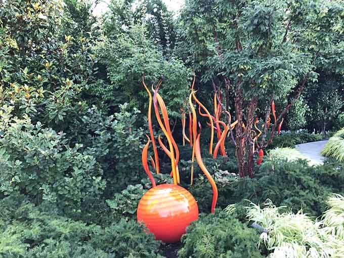 Fiery orange glass orbs and twisting blades tucked into greenery, like a garden that decided ordinary flowers were too boring.