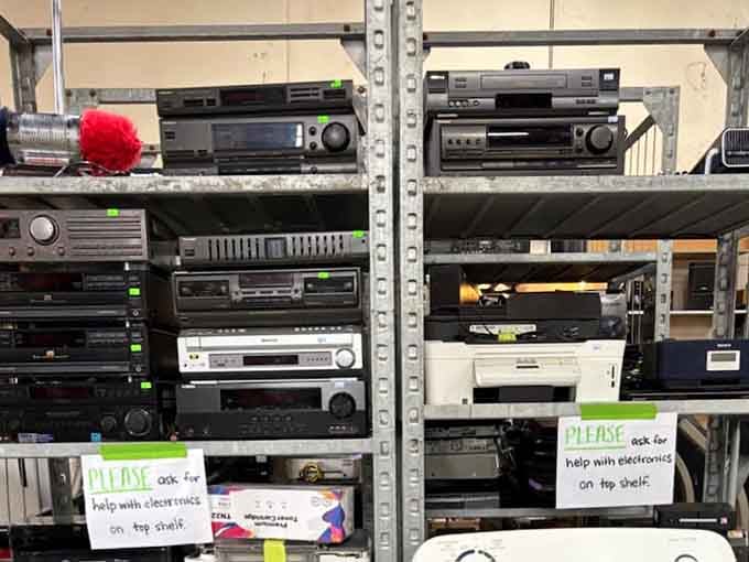 Vintage stereo receivers and electronics stacked high, with helpful signs reminding you to just ask for assistance.