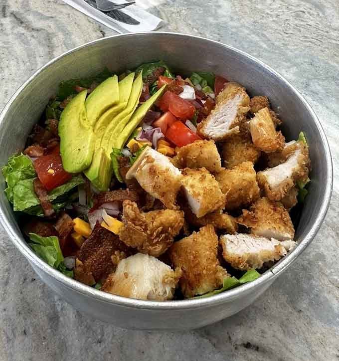 A crispy chicken salad bowl loaded with avocado and fresh vegetables, making healthy eating look downright irresistible for once.