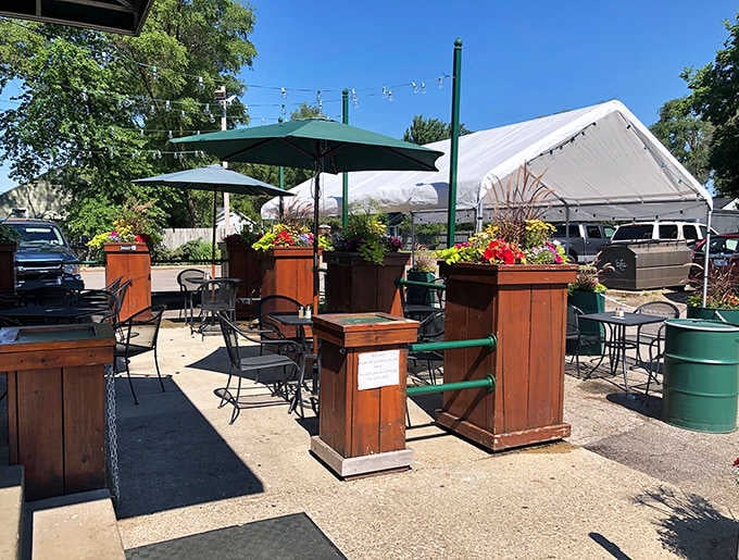 A sunny outdoor patio with flower planters, green umbrellas, and bistro chairs. Dagwood's even does fresh air with personality.