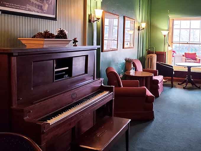 An upright piano, deep armchairs, and green walls that feel like a forgotten parlor from another era.