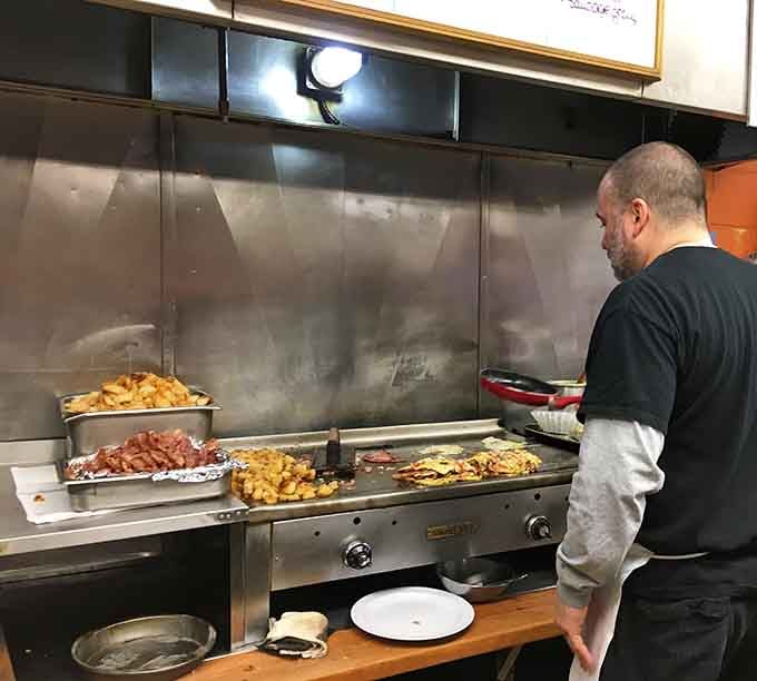The open griddle in full action, bacon sizzling and home fries crisping, the most honest kitchen you'll ever see.