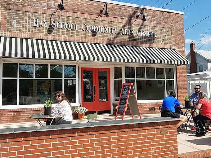 The Bay School Community Arts Center: red doors, striped awnings, and people sitting outside who clearly made very good decisions today.