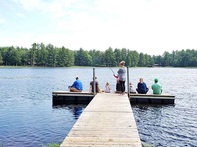 A family lined up on the dock with fishing poles dangling over calm blue water, this is what a perfect afternoon actually looks like.