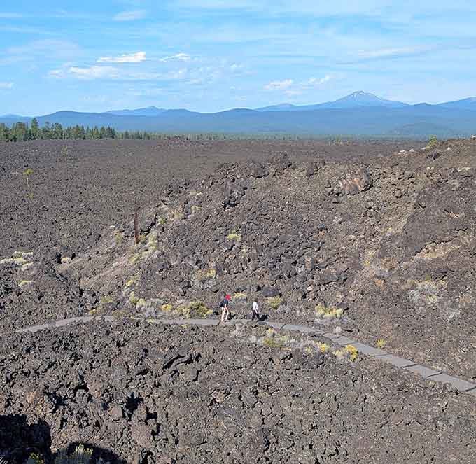 Two tiny hikers crossing a vast lava plain, with the Cascades watching from a comfortable distance behind them.