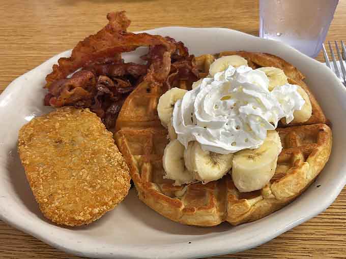 A Belgian waffle topped with banana slices and whipped cream, with crispy bacon alongside. Sweet, savory, and completely worth every bite.
