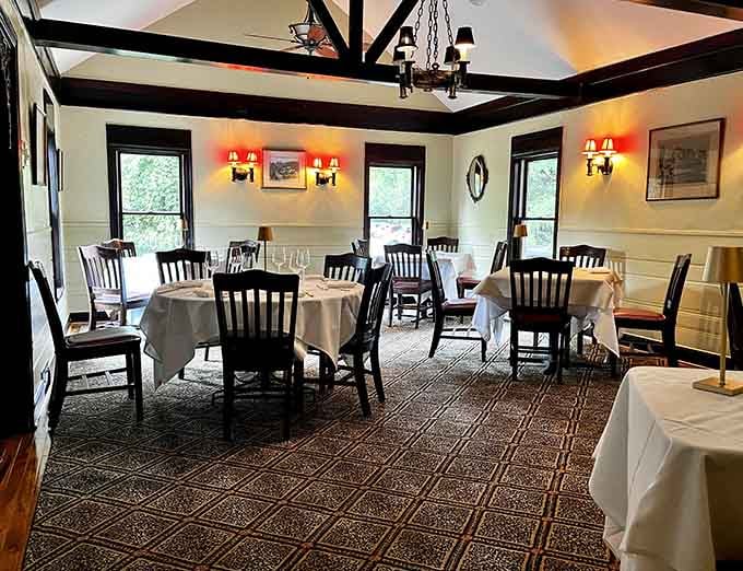Warm sconce lighting, exposed dark beams, and white-draped tables give this dining room a cozy, unhurried elegance all its own.