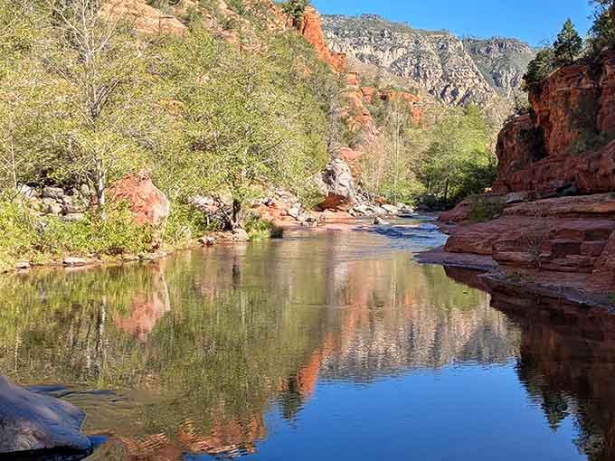 Still water reflecting red canyon walls and green trees, the kind of mirror that makes you stop and stare.