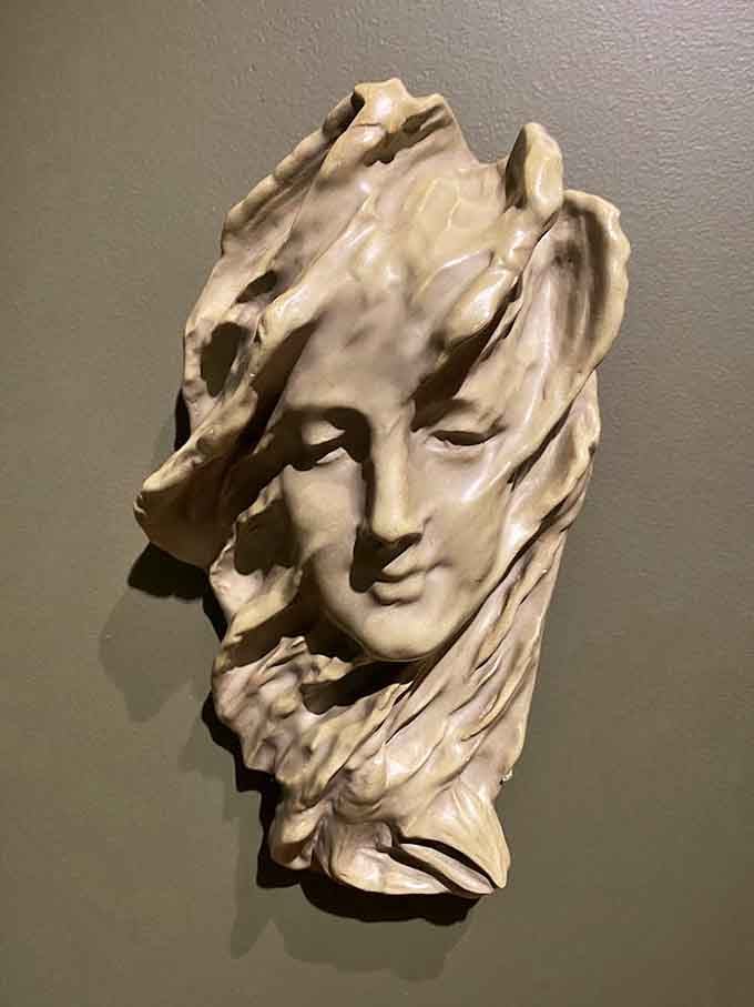 That serene ceramic face emerging from swirling drapery folds watches you from the wall with the calm confidence of someone who knows all your secrets.