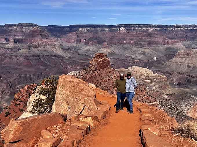 Two visitors walking the red dirt path with the entire canyon spread behind them, looking appropriately thrilled about their life choices.