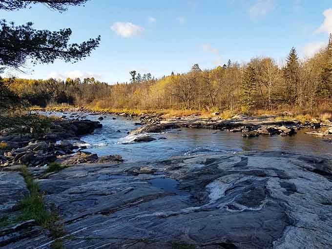 Cool blue water winds through the rugged terrain, surrounded by the quiet beauty of the forest in the afternoon light.