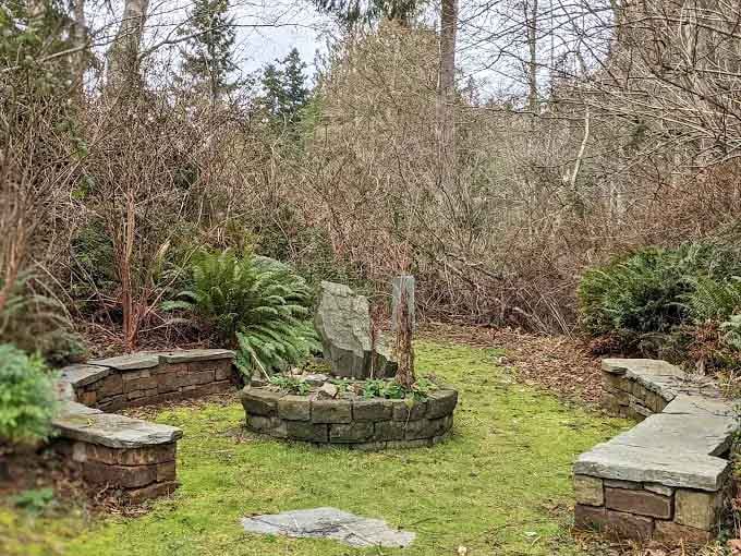 Mossy stone walls cradle a small garden bed with a standing rock at its center, creating a peaceful nook that feels genuinely timeless in winter's bare light.