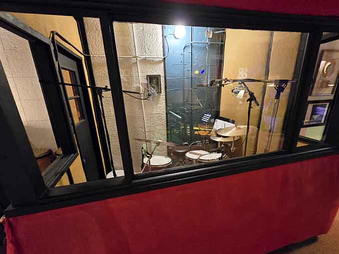 Through the glass, a drum kit sits in the isolation booth, mic'd up and ready, just like it always was.