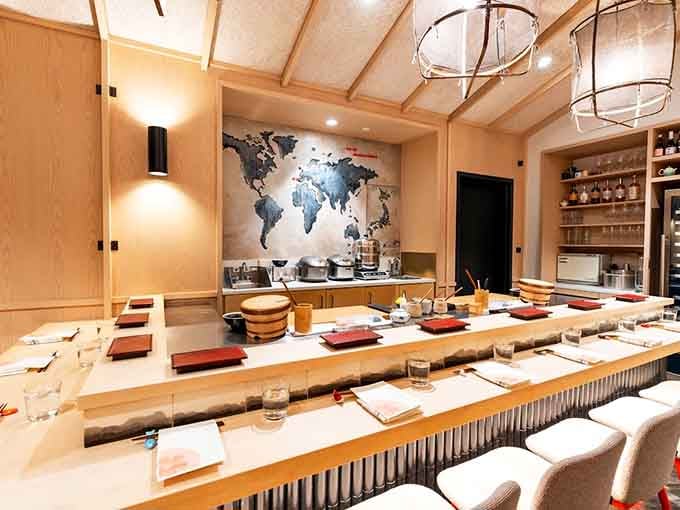 Place settings lined up along the pale counter, red mats waiting, glasses ready, the whole room holding its breath before the first course arrives.
