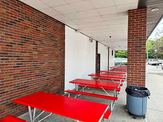 Bright red picnic tables lined up under a covered brick overhang, casual outdoor dining that suits a clam bar perfectly.