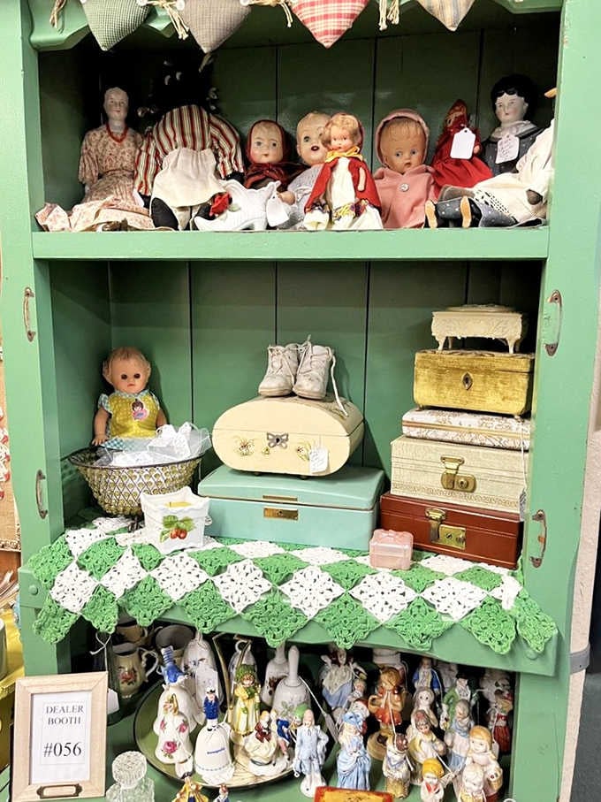 A mint green cabinet packed with antique dolls, tiny shoes, vintage cases, and porcelain figurines, charming and wonderfully overstuffed all at once.