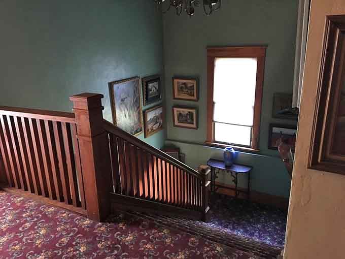 A handsome wooden staircase lined with framed artwork and floral carpet, climbing upward like the opening scene of a very good novel.