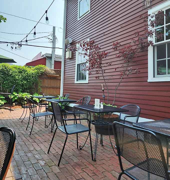 Brick patio, string lights overhead, and black iron chairs tucked beside lush greenery, the kind of outdoor spot worth lingering over.