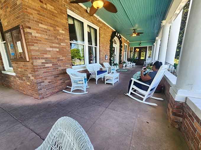 White wicker chairs and rocking chairs lining a teal-ceilinged wraparound porch, the kind of spot where time genuinely slows down.