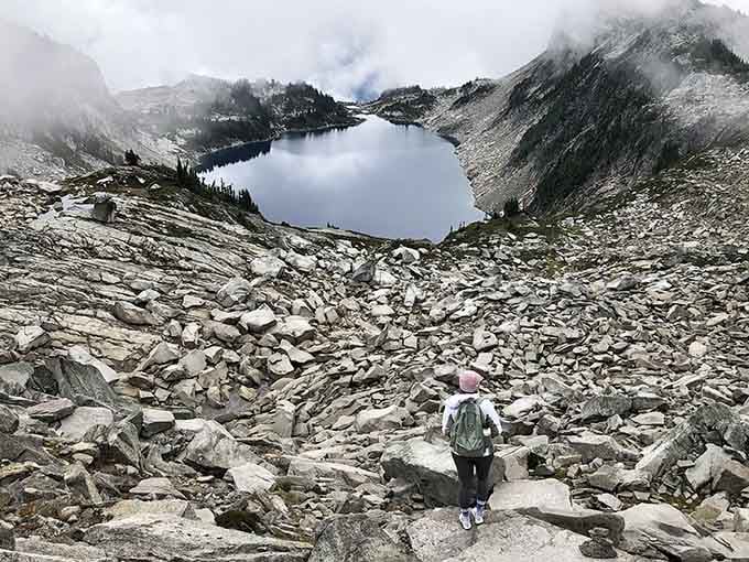 One determined hiker, a field of boulders, and a misty alpine lake waiting patiently below like a reward well earned.