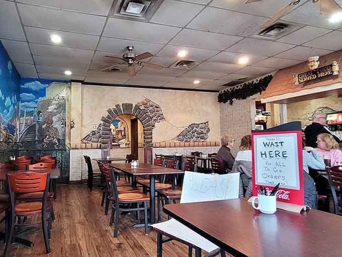 Italian village murals, wooden chairs, and ceiling fans spinning lazily overhead. This dining room means serious, comfortable business.